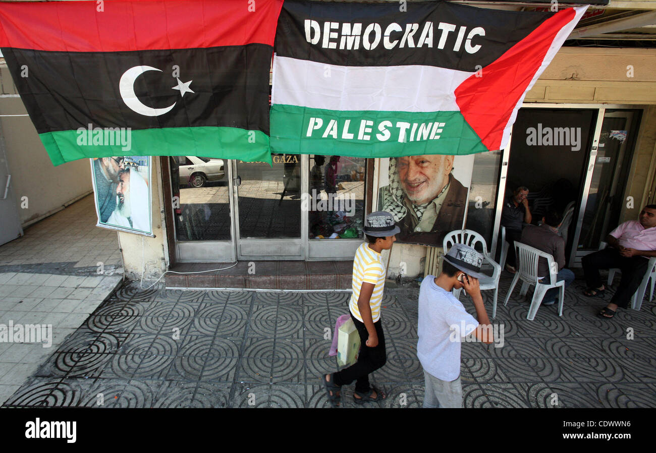 Palestinian people walk past a Libyan rebel flag in front of a shop in ...