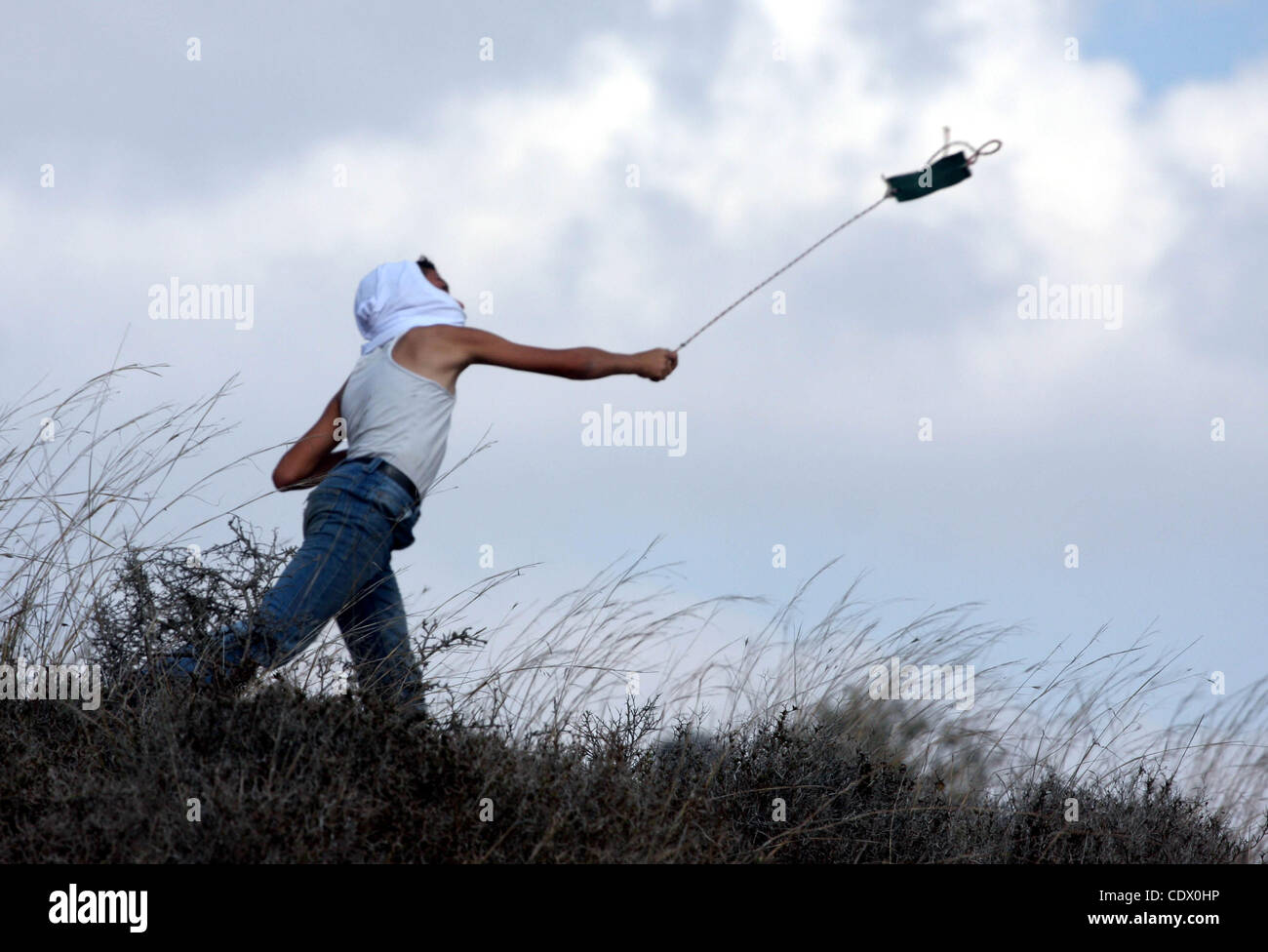 A Palestinian youth uses a sling to hurl stones towards Israeli ...
