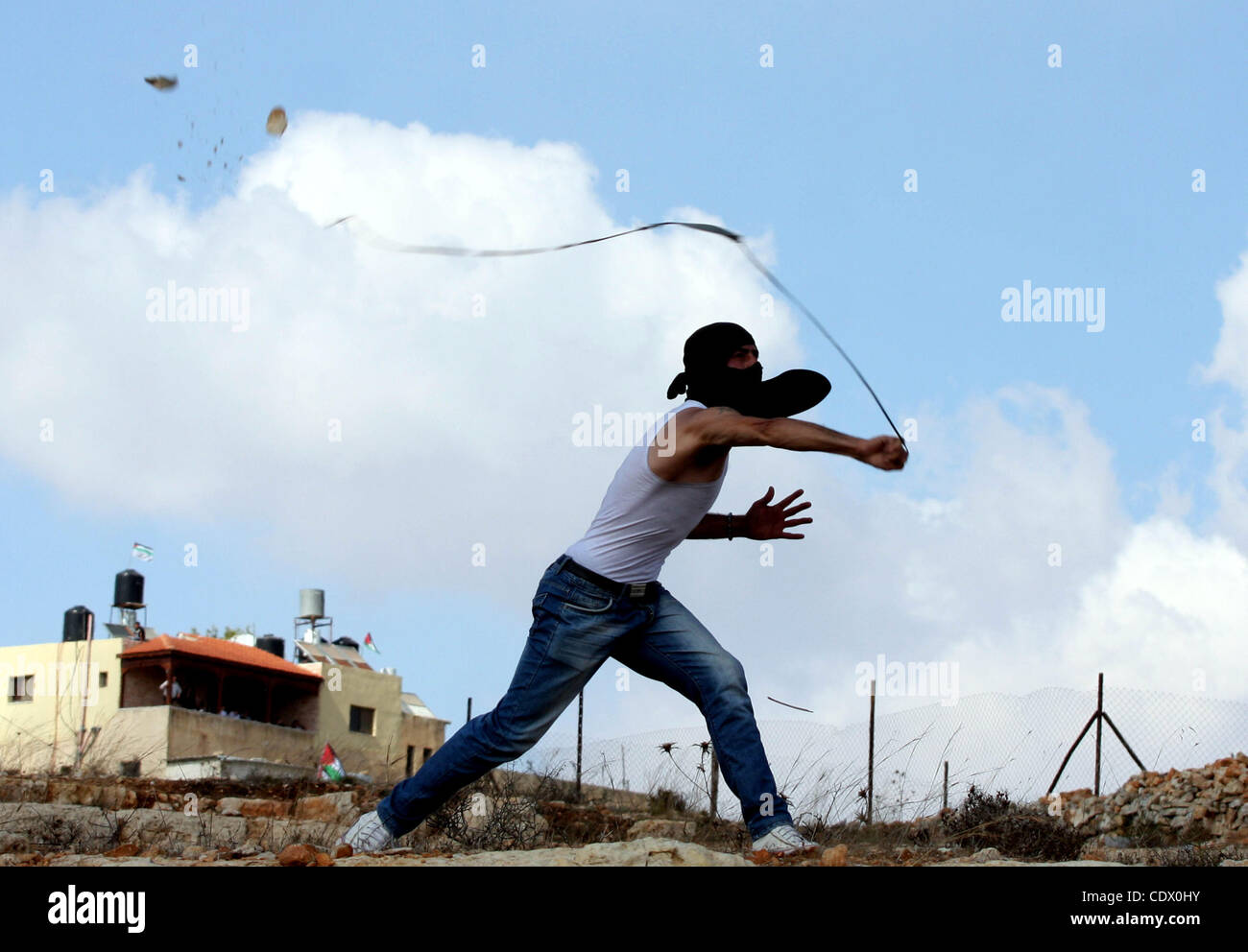 A Palestinian youth uses a sling to hurl stones towards Israeli ...
