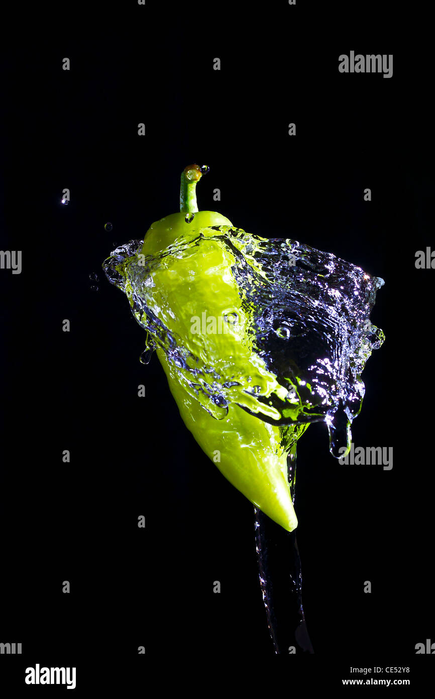 Green pepper splashed by water over black background Stock Photo - Alamy