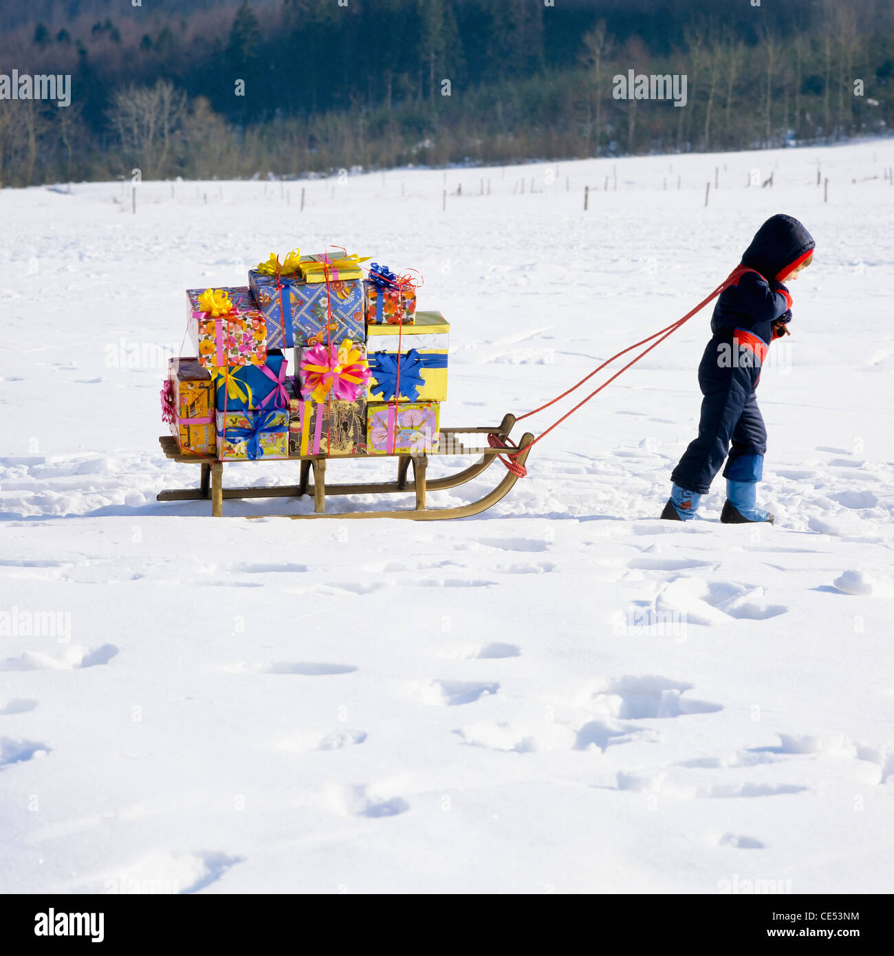 Little boy pulling a sledge loaded with Christmas presents in snow ...