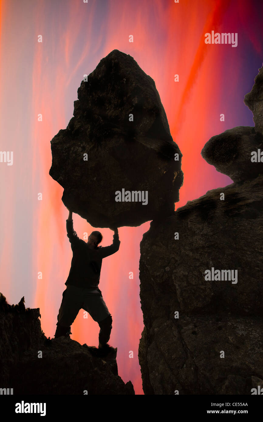 A climber lifting a huge boulder on Dow Crag at sunset, Lake District ...