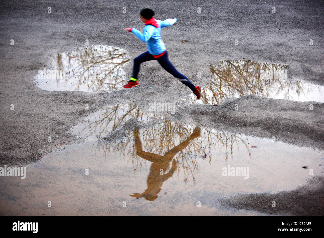 2 young women running in winter, jumping over wet spots on the way ...