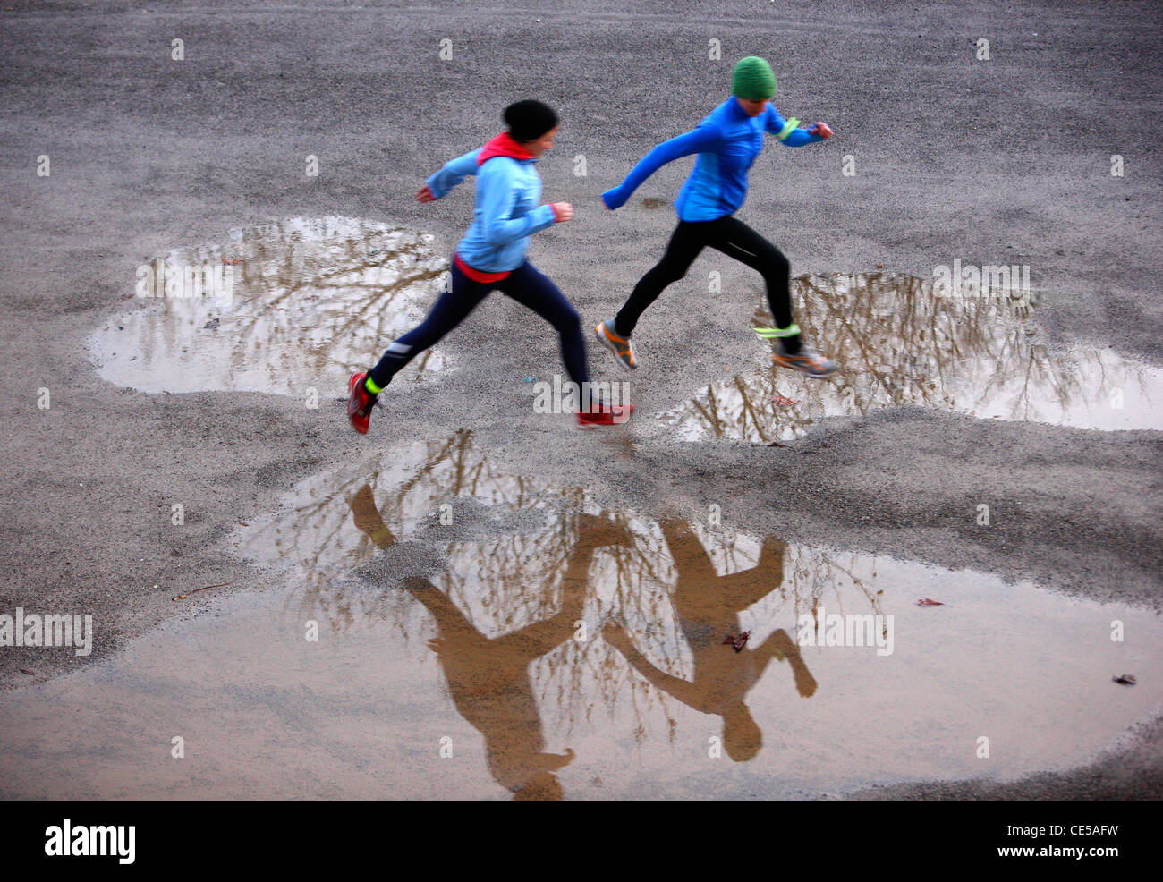 2 young women running in winter, jumping over wet spots on the way ...