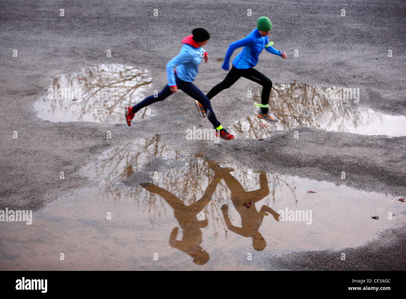 2 young women running in winter, jumping over wet spots on the way ...