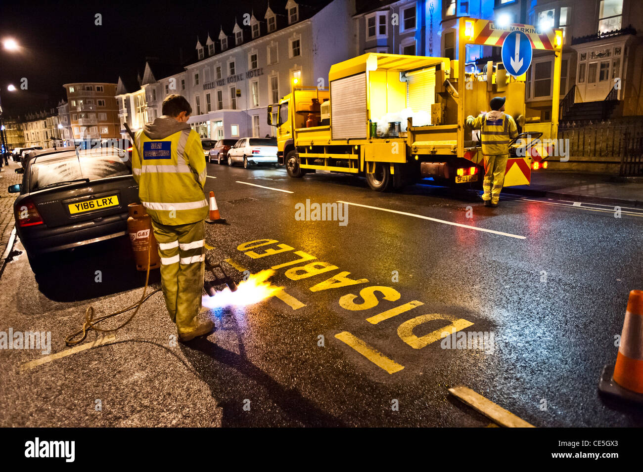 Men working using a flame gun setting out road markings at night on a ...