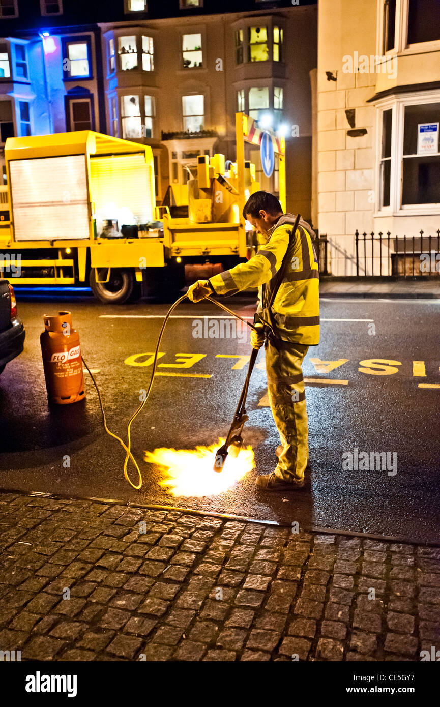 Men working using a flame gun setting out road markings at night on a ...