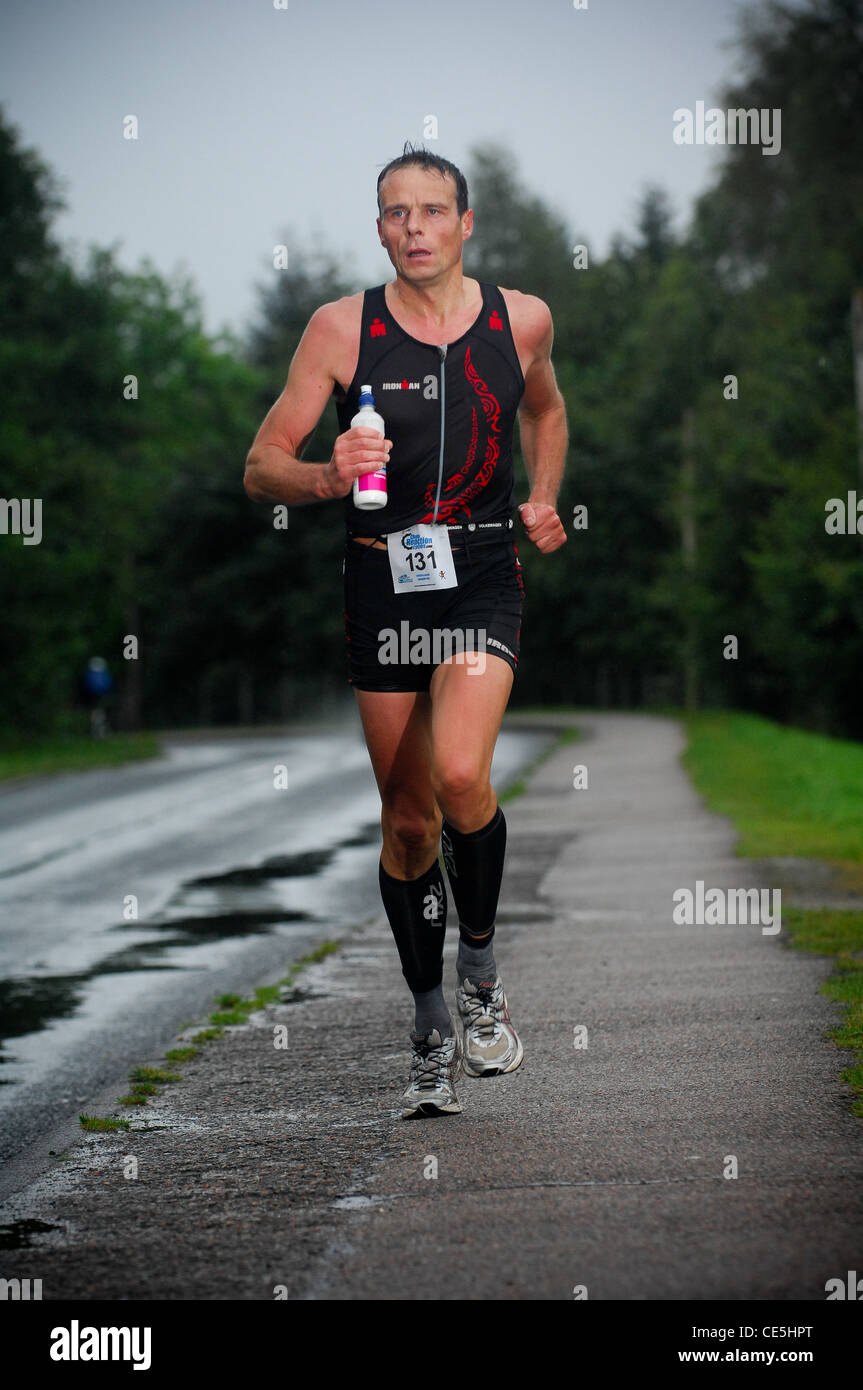 Triathlon competitors running down empty wet road with puddles and rain ...