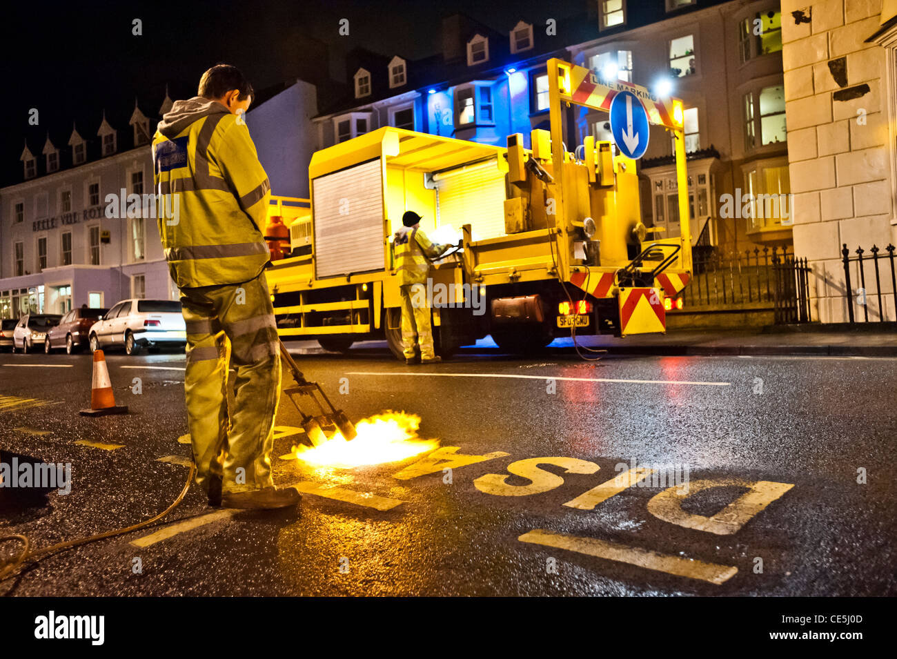 Men working using a flame gun setting out road markings at night on a ...