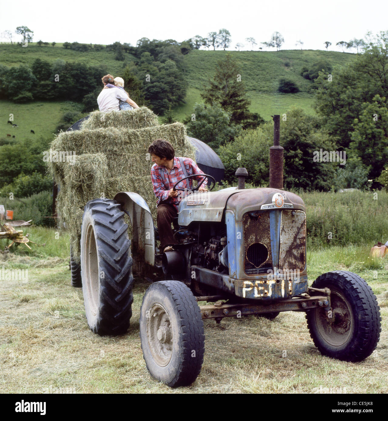 Man farmer with people sitting on top of hay bales on a trailor at ...