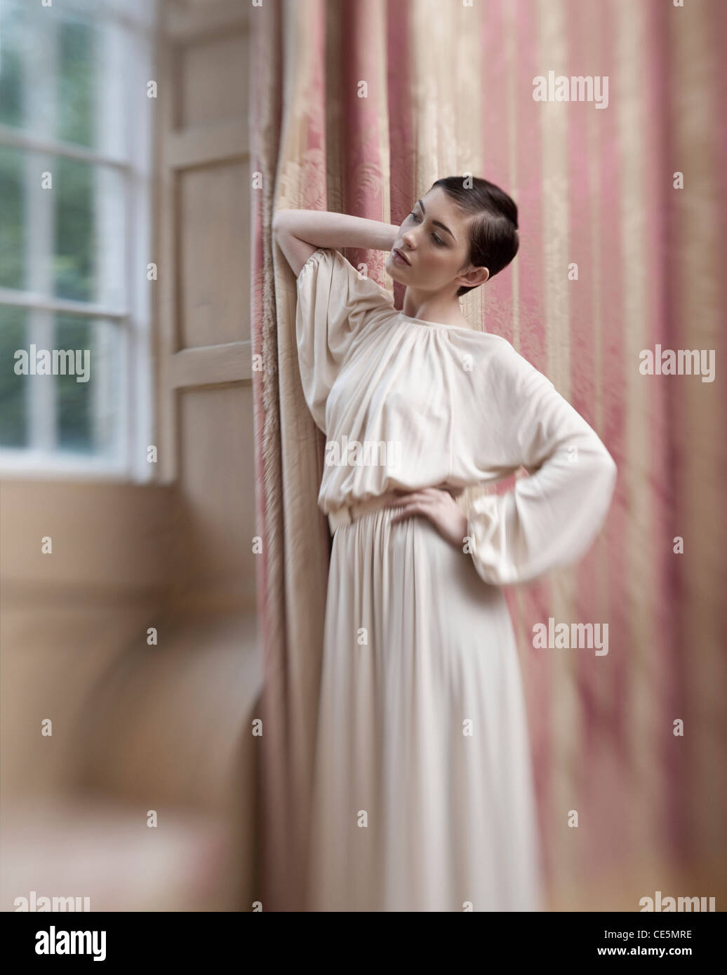 A woman standing by a window, wearing a long dress Stock Photo - Alamy