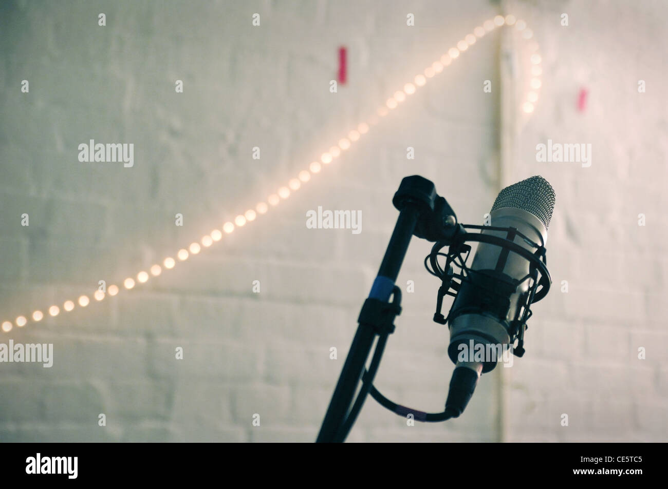 A studio microphone with a trail of lights behind on a white brick wall ...