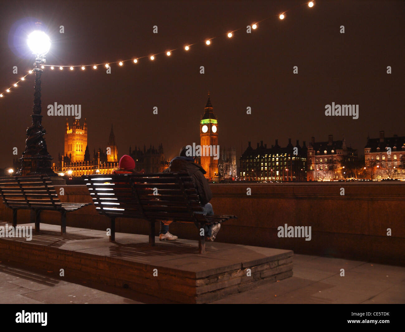 Tourists sit on a bencj on London's South Bank and take in a view of ...