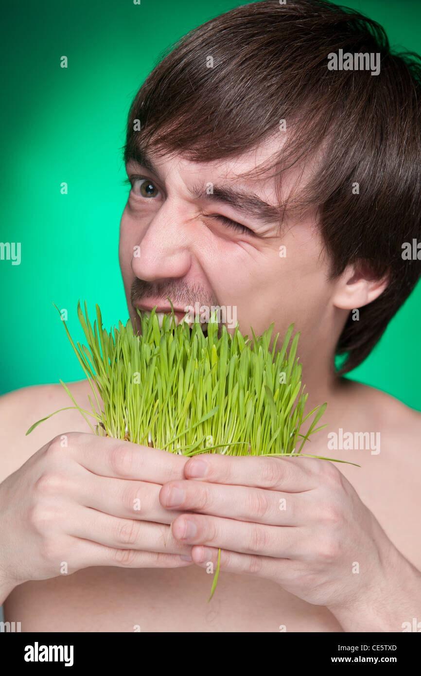 Young man eating a bunch of fresh green grass on a green background ...