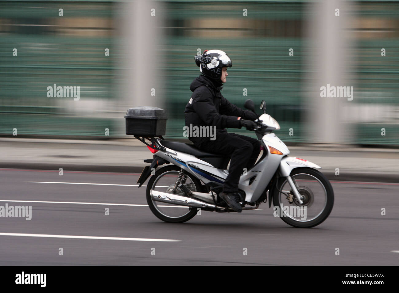 a moped and rider traveling along a road in London Stock Photo - Alamy