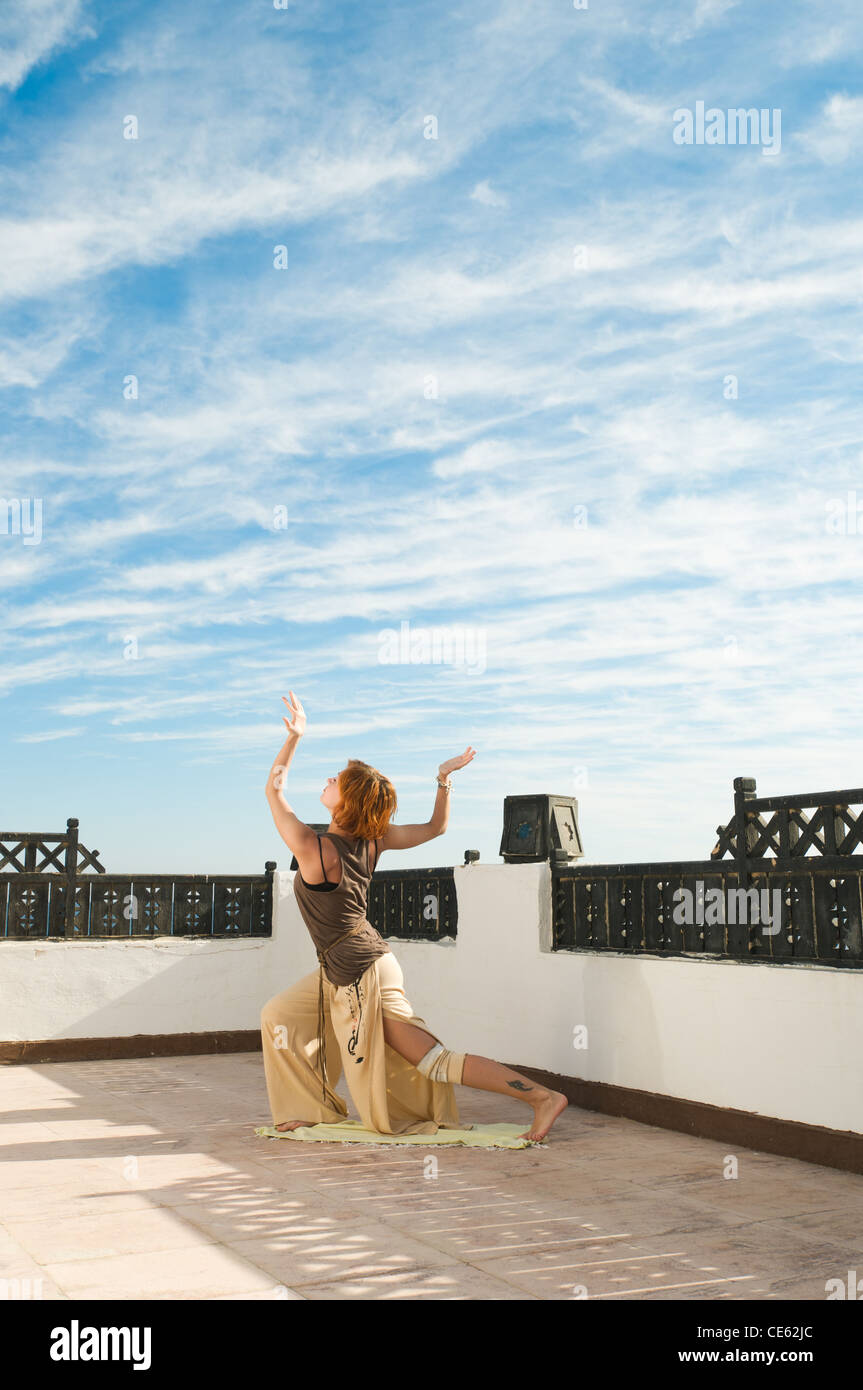 Beautiful young dancer performing yoga-dance outdoors with blue sky and ...