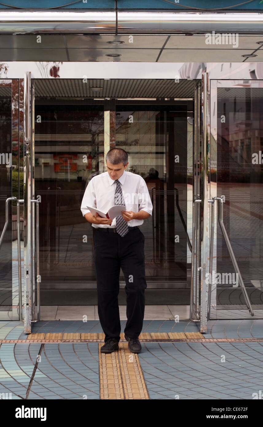 A man reading something from a notebook while walking out from a modern ...