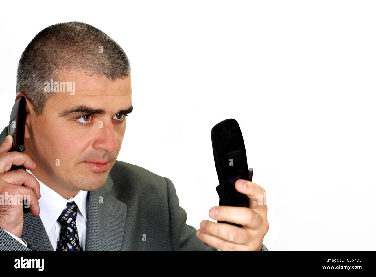 Portrait of a very busy businessman using two mobile phones:one for ...