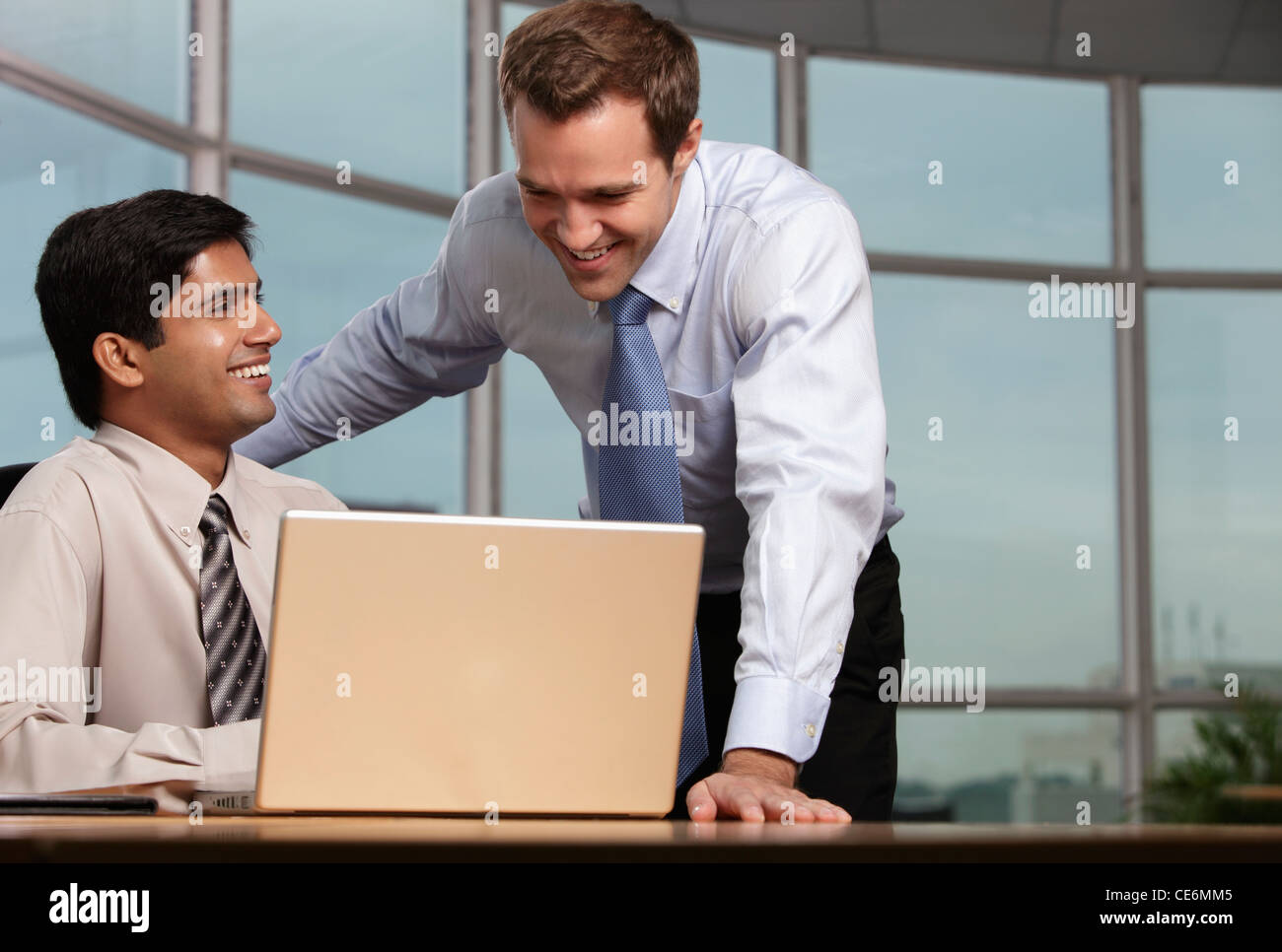 Caucasian man looking at laptop with Indian man and smiling Stock Photo ...