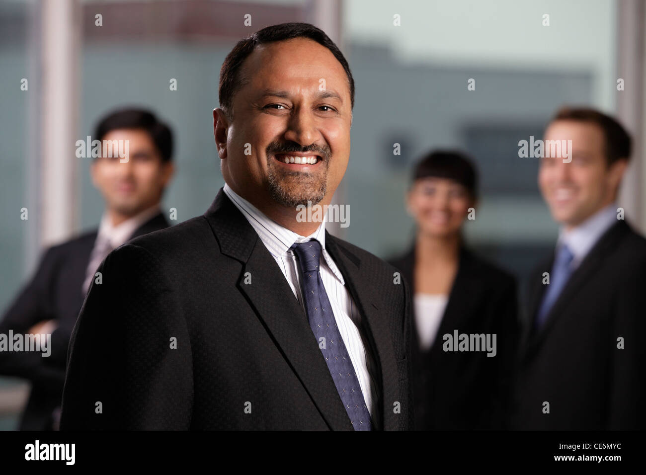 Indian man smiling at camera with colleagues behind him Stock Photo - Alamy