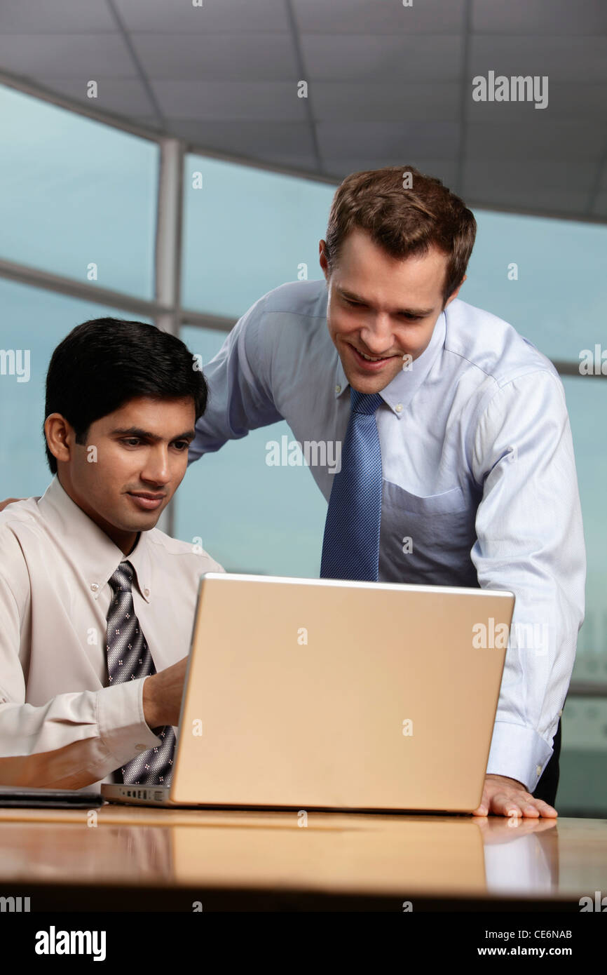 Caucasian man looking at laptop with Indian man Stock Photo - Alamy