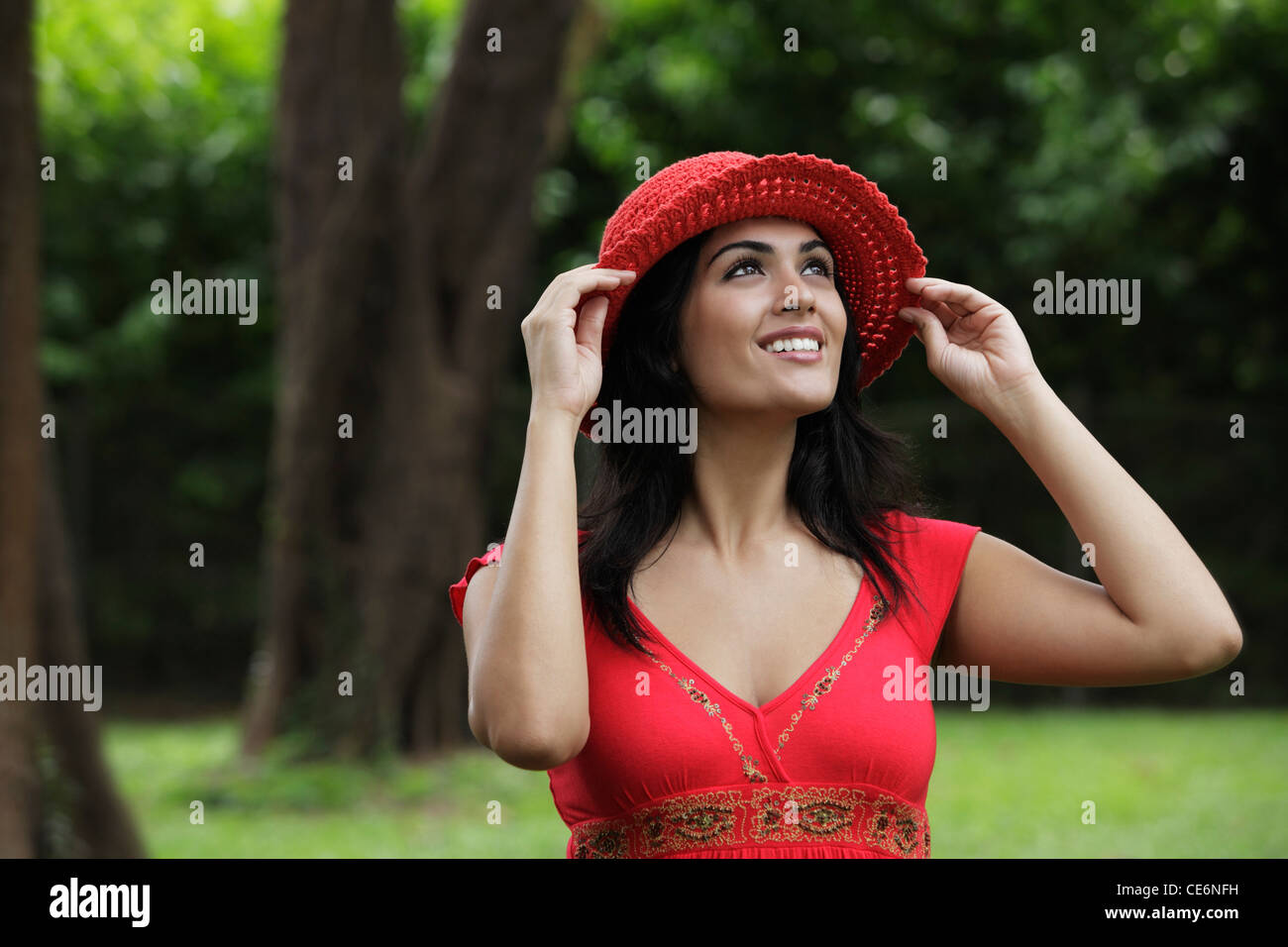 Half shot of woman wearing a red hat looking up, trees as background ...