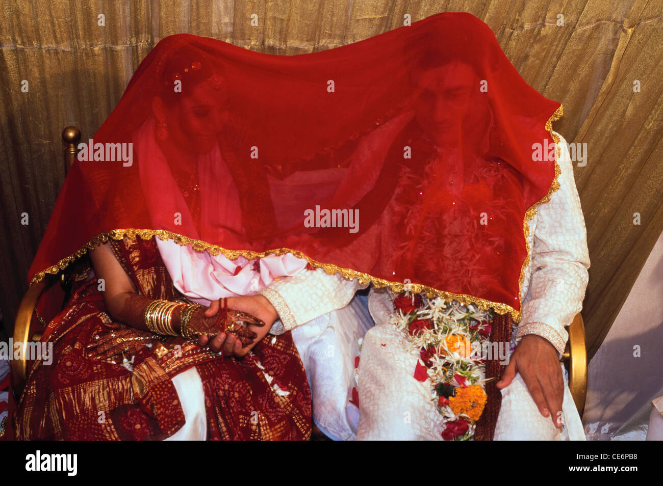 Bride and bridegroom holding hands and face covered by red cloth in ...