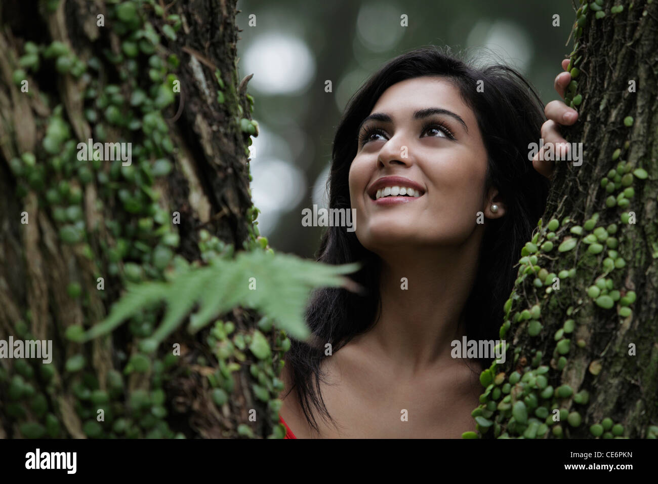 Head shot of young woman looking through a tree and smiling Stock Photo ...