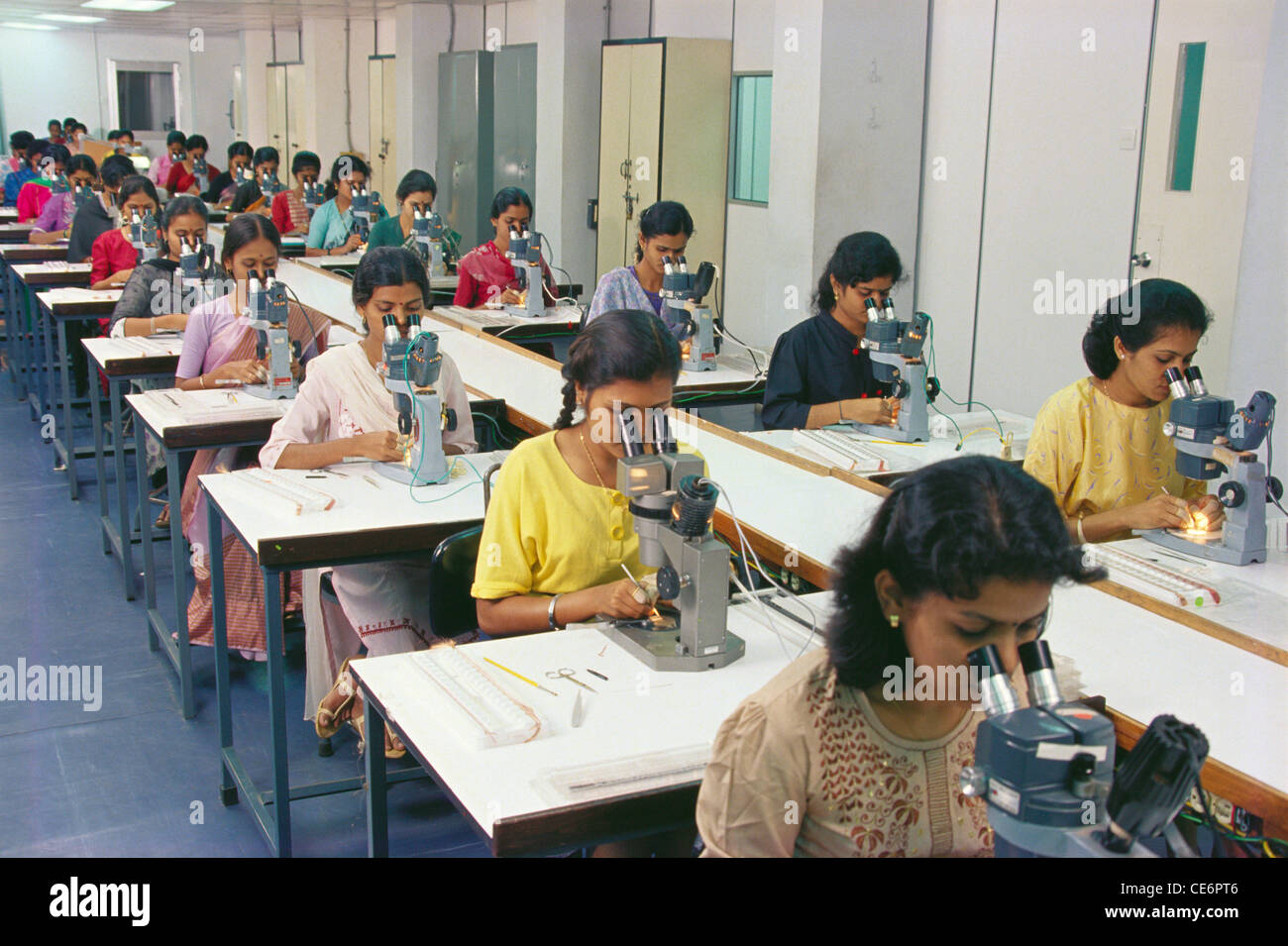 Indian women workers looking through microscopes working in electronics ...