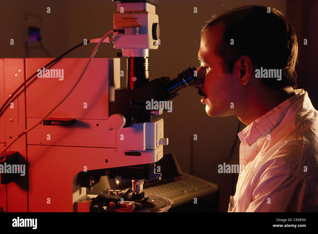 Indian man looking through microscope working in electronic industry ...