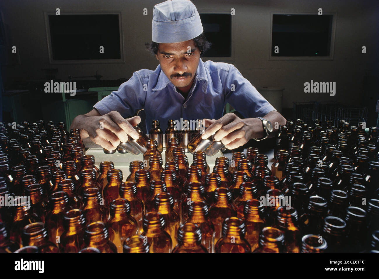 Indian worker in cap checking handling glass bottles in glass factory ...