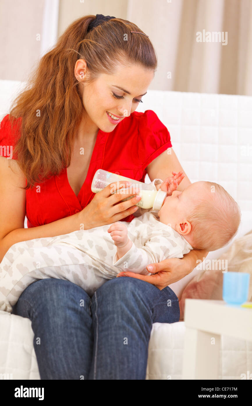 Happy mother sitting on sofa and feeding baby Stock Photo - Alamy