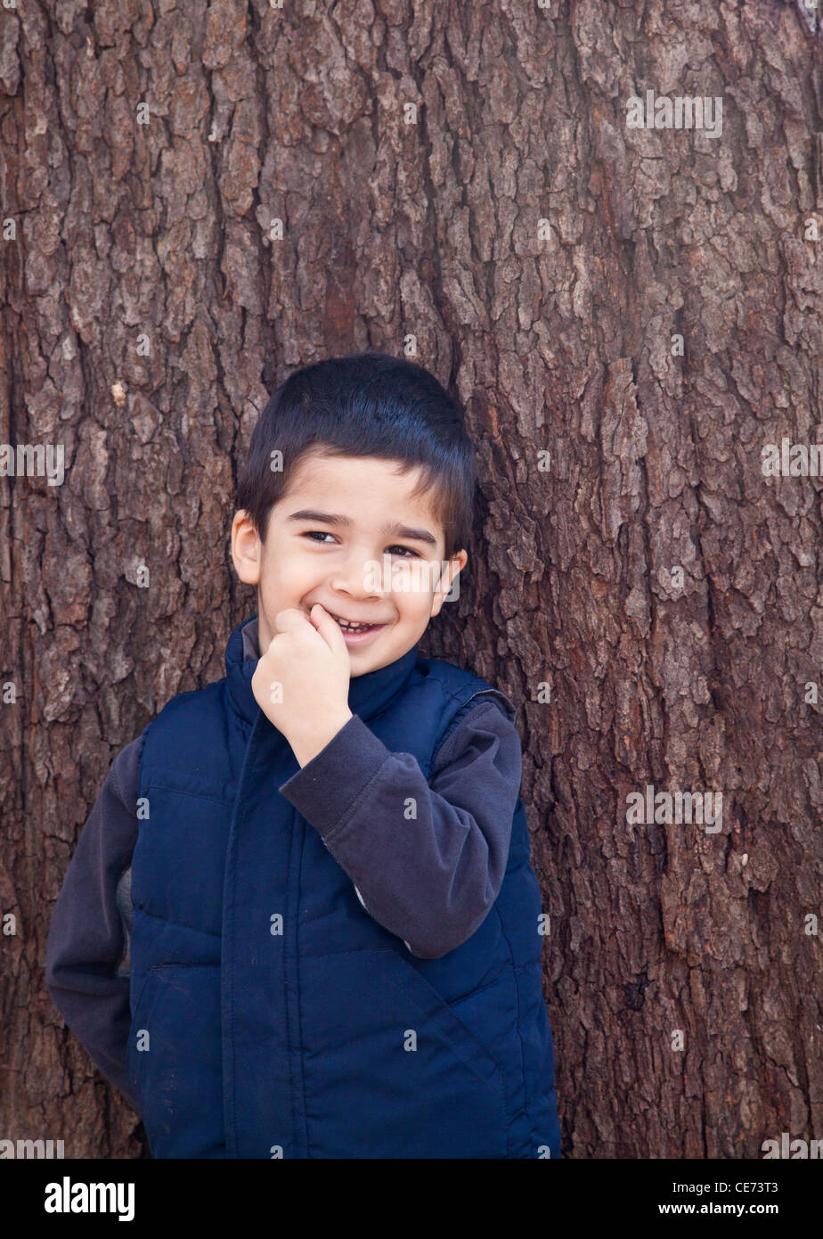 Little boy looking to the left in front of a tree with bark texture in ...