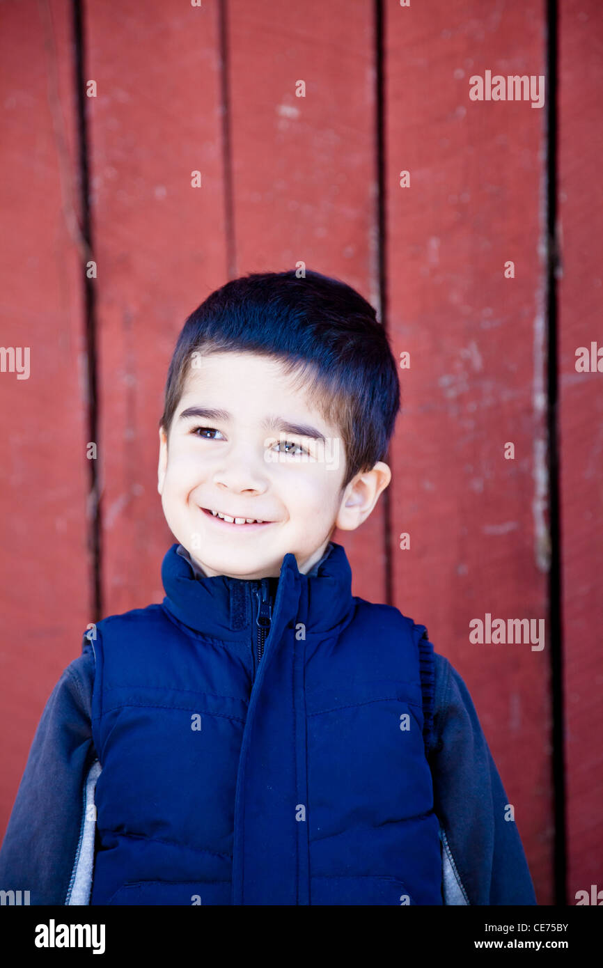 Little boy looking up and to the left in front of red textured ...