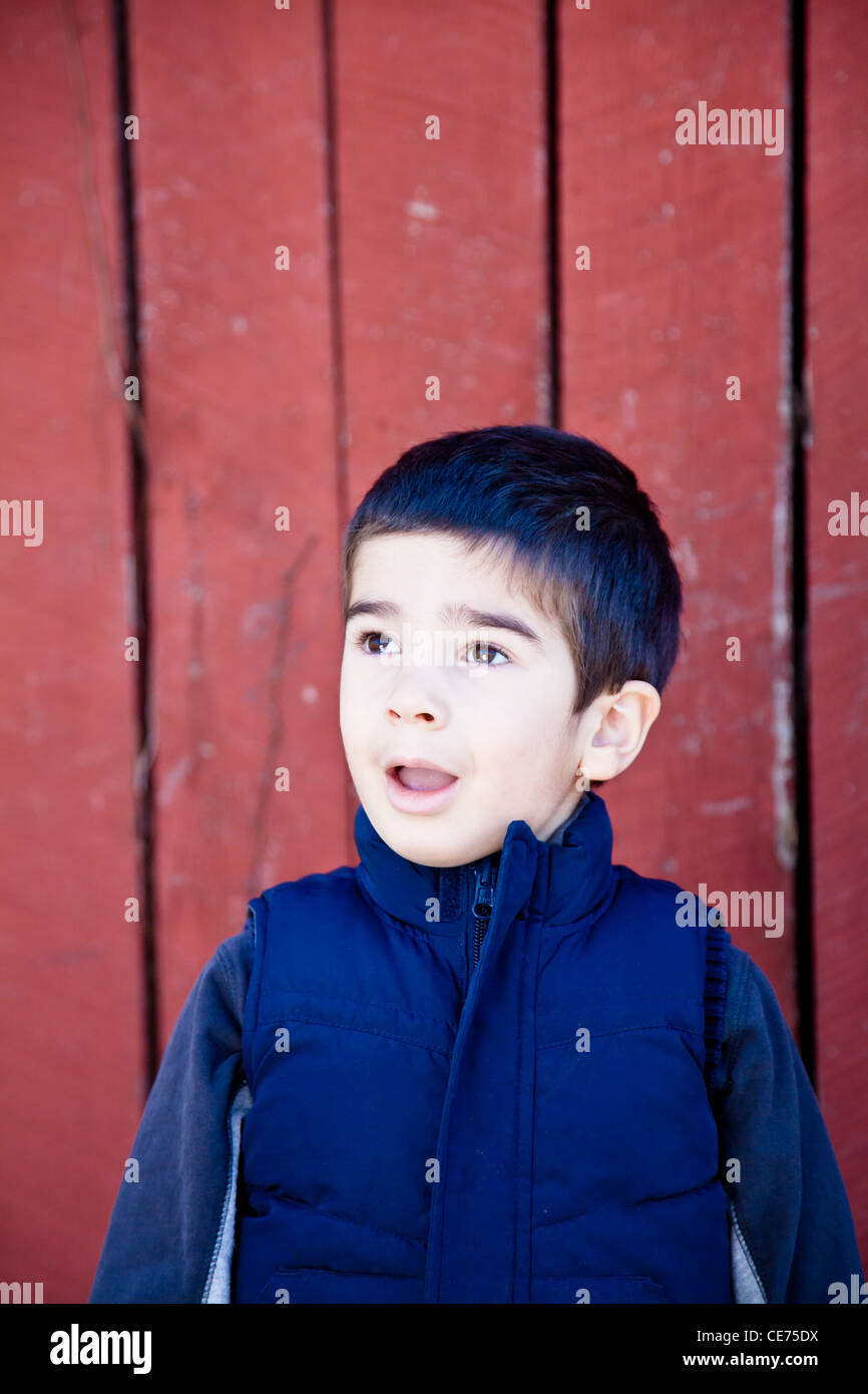 Little boy looking up and to the left in front of red textured ...
