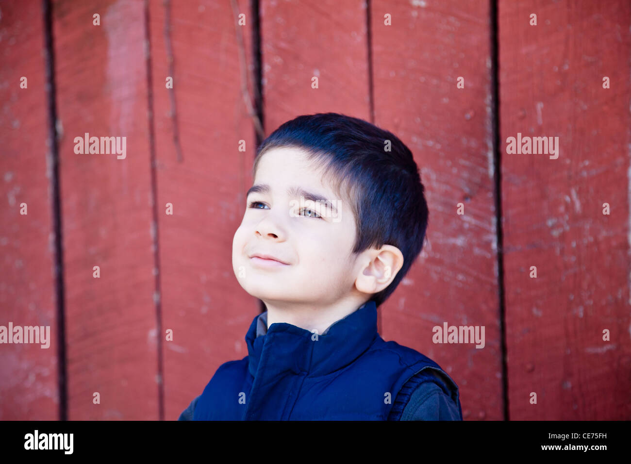 Little boy looking up and to the left in front of red textured ...
