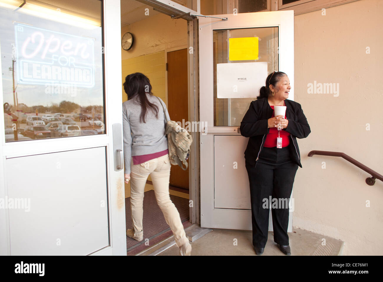 Hispanic teacher welcomes students to school at the entrance door of ...