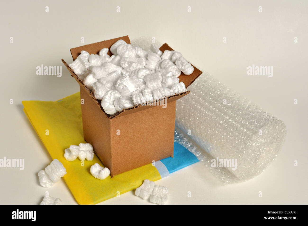 A brown cardboard box sits on top of tissue paper with shipping peanuts ...