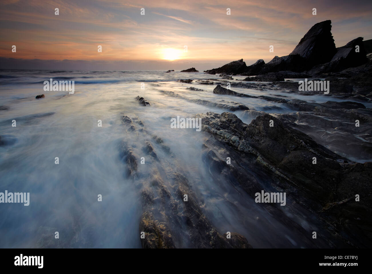 Low evening sunlight illuminates the rocks in Westcombe bay as the tide ...
