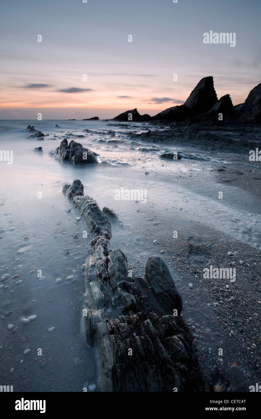 Low evening sunlight illuminates the rocks in Westcombe bay as the tide ...