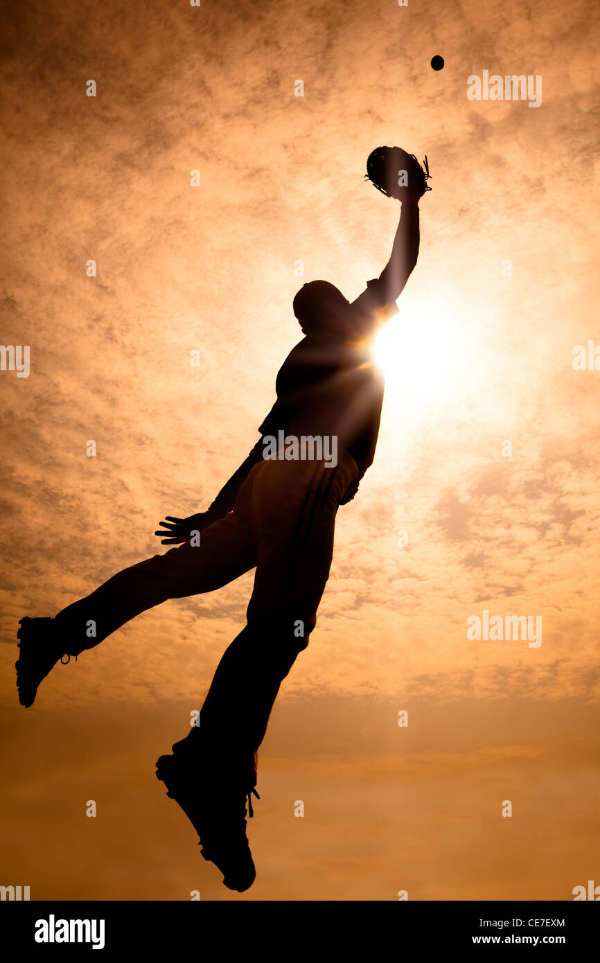 The silhouette of baseball player jumping into air to make the catch ...