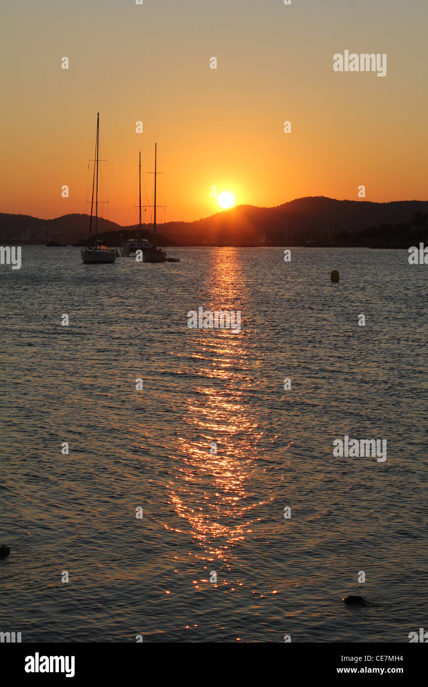 Coastal scene at evening - sailing yachts at anchor in setting sun with ...