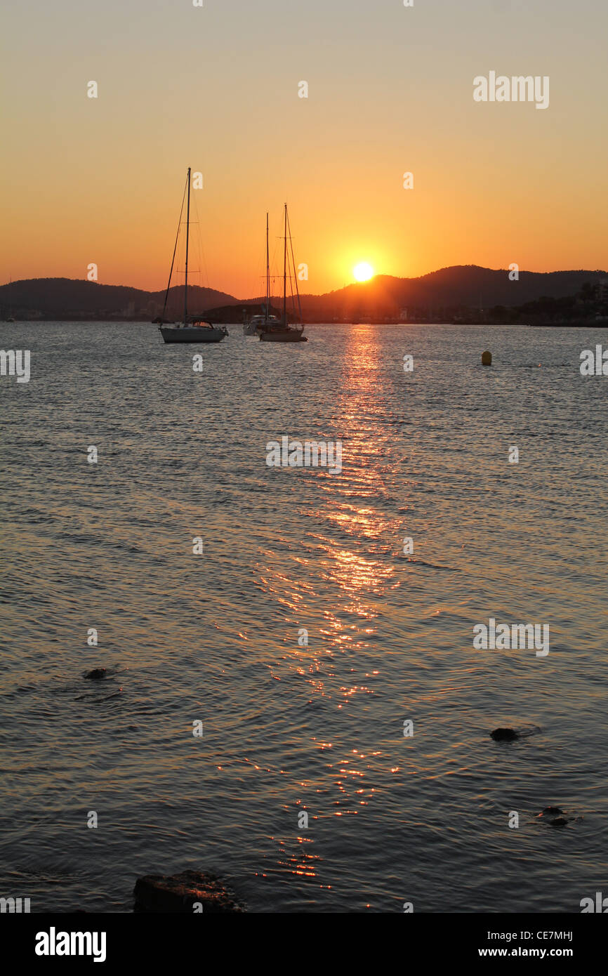 Coastal scene at evening - sailing yachts at anchor in setting sun with ...