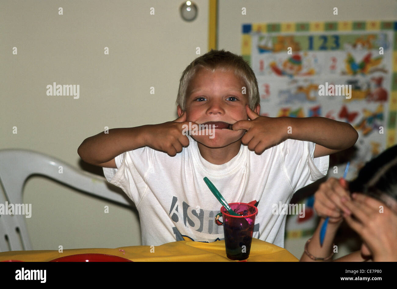 Young boy sitting at table pulling faces Stock Photo - Alamy