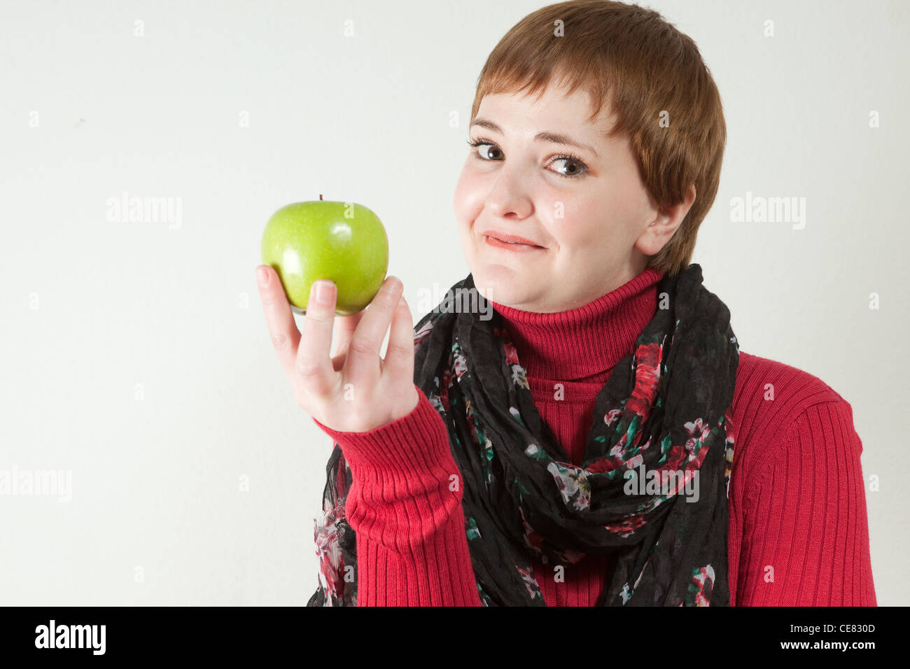 Young redhaired woman holding green apple in front of her, with ...