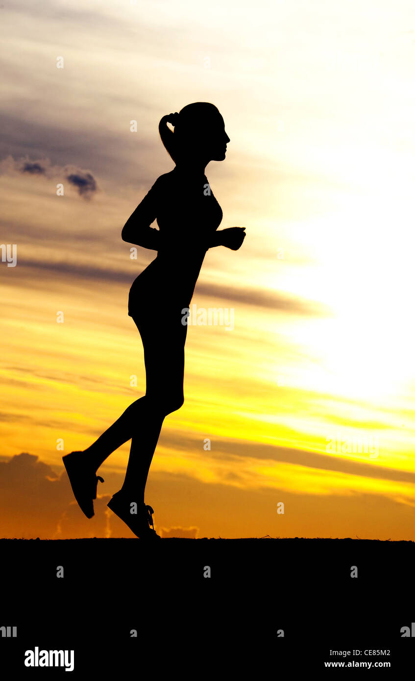 Silhouette of a beautiful running woman against yellow sky with clouds ...