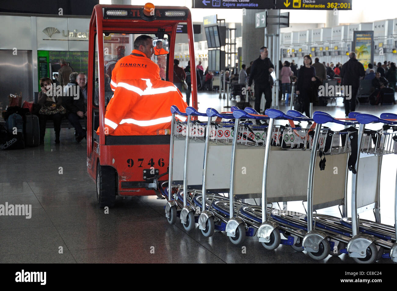 Worker collecting a row of luggage trolleys inside Terminal 3, Malaga ...