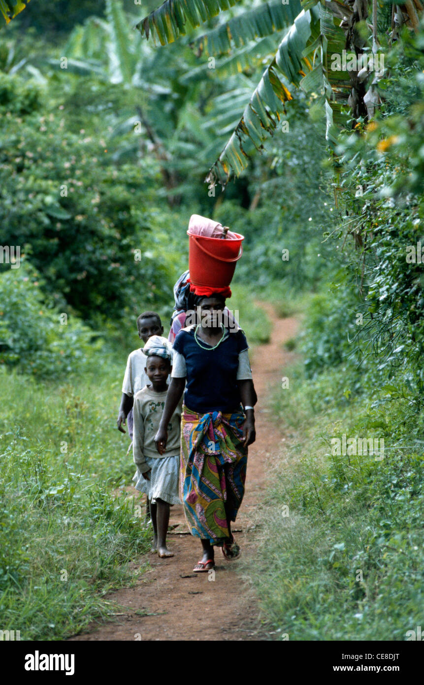 Woman carrying bucket on her head and children following in rural ...