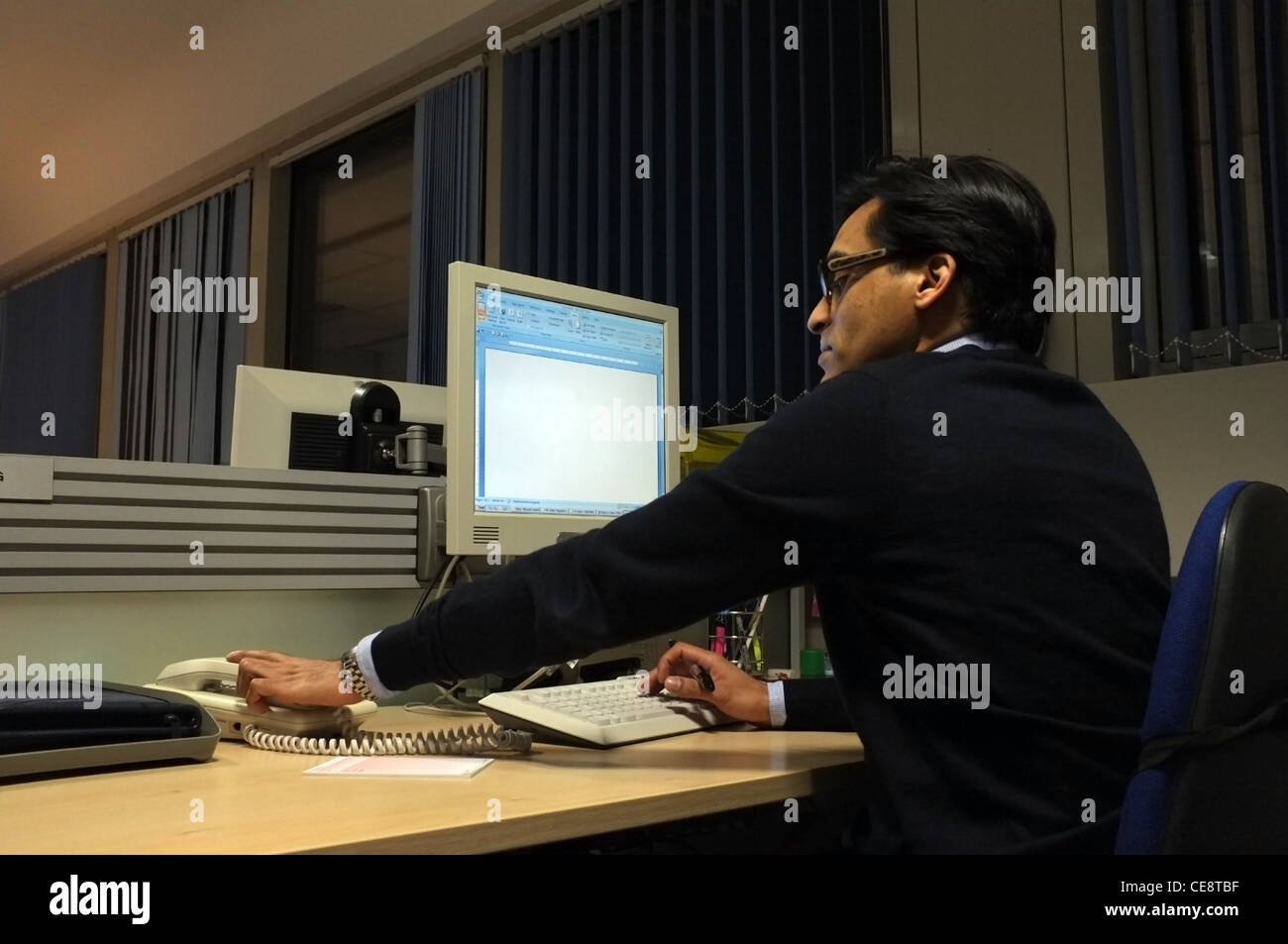 An office worker, at computer, is about to pick up a ringing phone ...