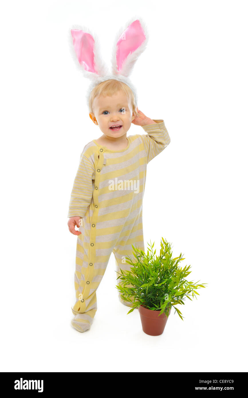 Cute baby with rabbit ears standing near pot with a plant isolated on ...